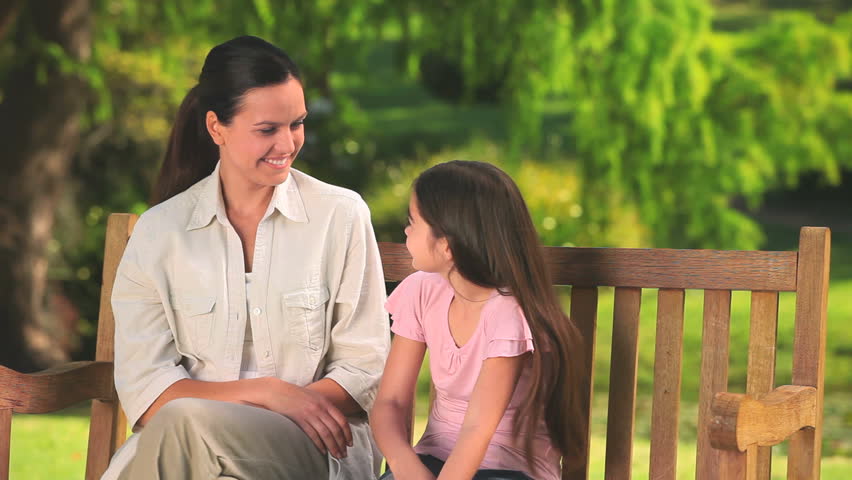 Mother Talking To Her Daughter While Sitting On A Park Bench Stock