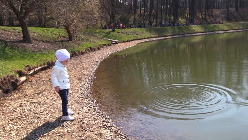 Girl on the bank throws a stone into the lake and washes hands in water ...